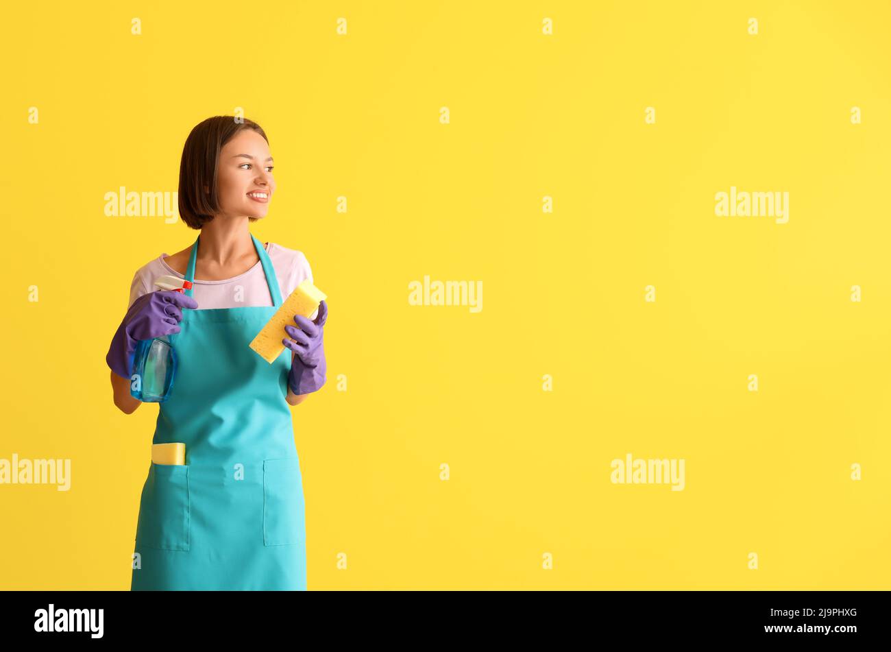 Young woman with cleaning sponge and bottle of detergent on yellow ...