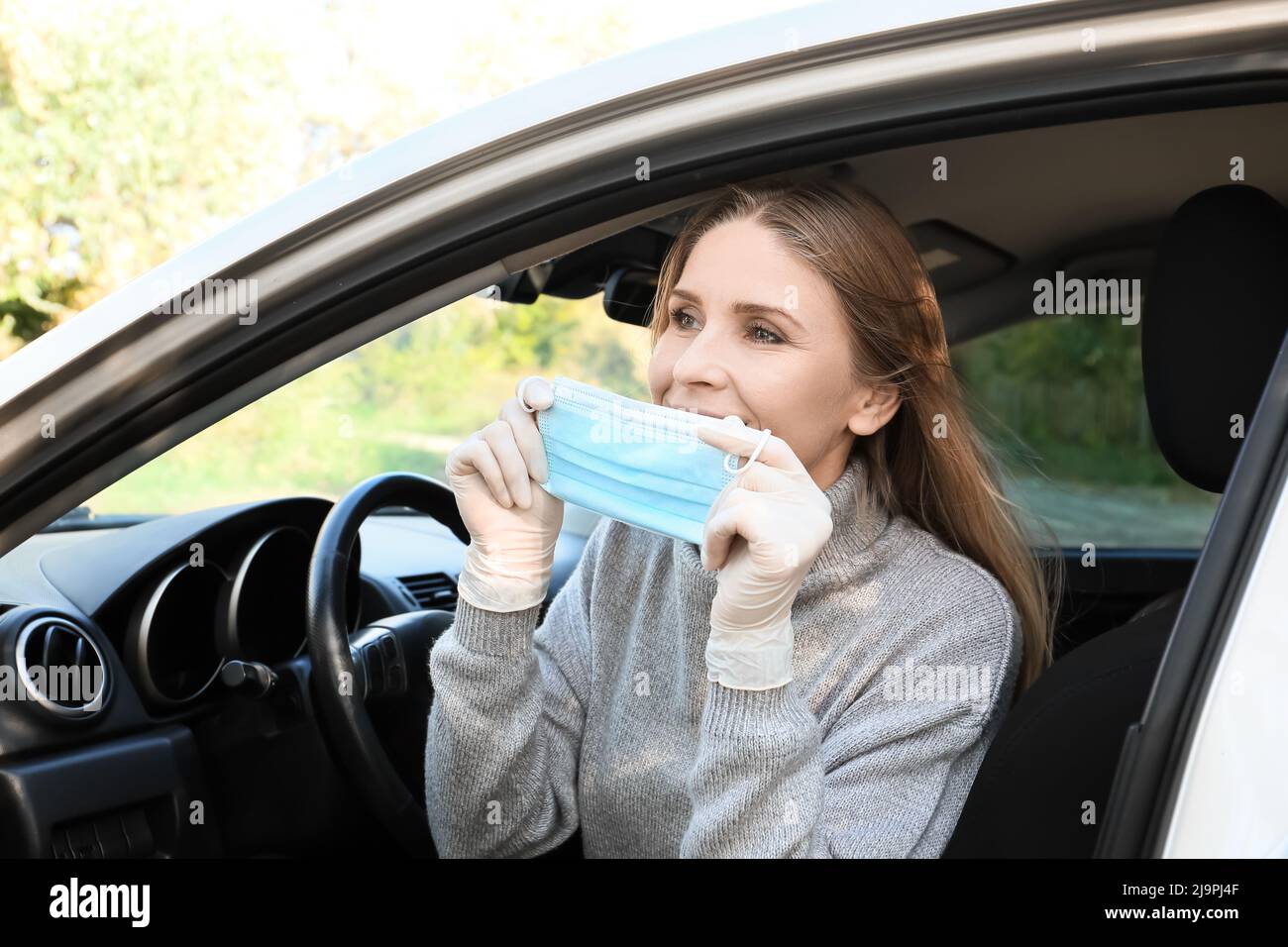 Female driver putting on medical mask and getting out of car Stock ...