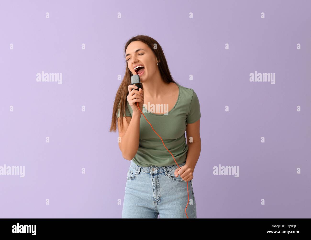 Pretty young woman with microphone singing on lilac background Stock ...