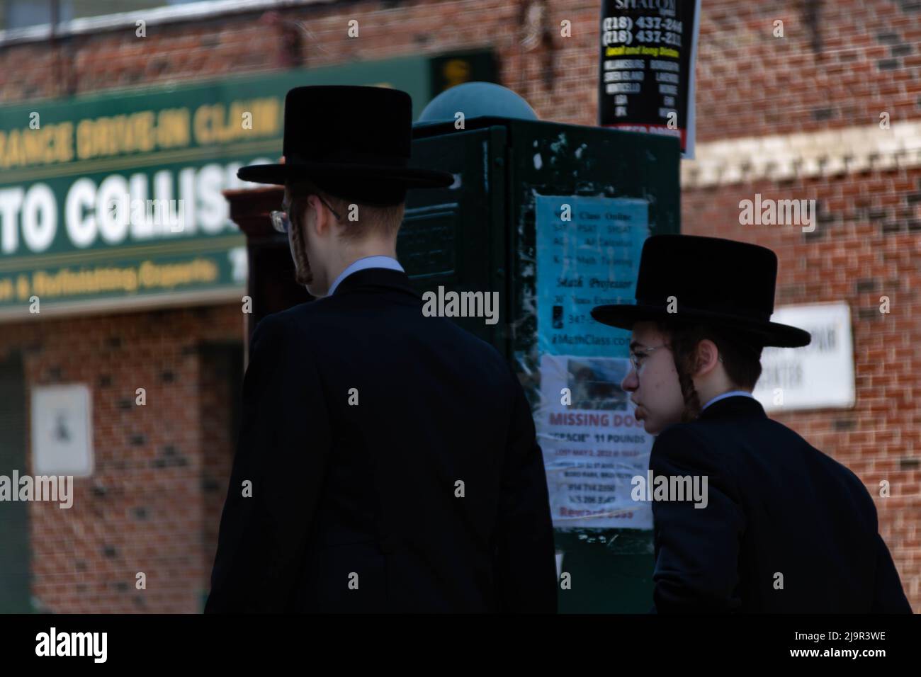 Two young orthodox Jewish men wearing hats are walking on the street ...