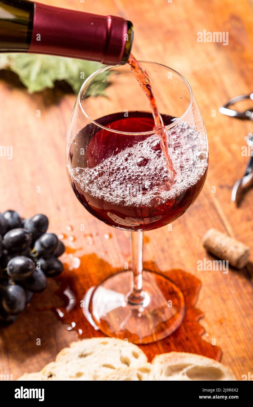 Pouring red wine glass against wooden background Stock Photo - Alamy