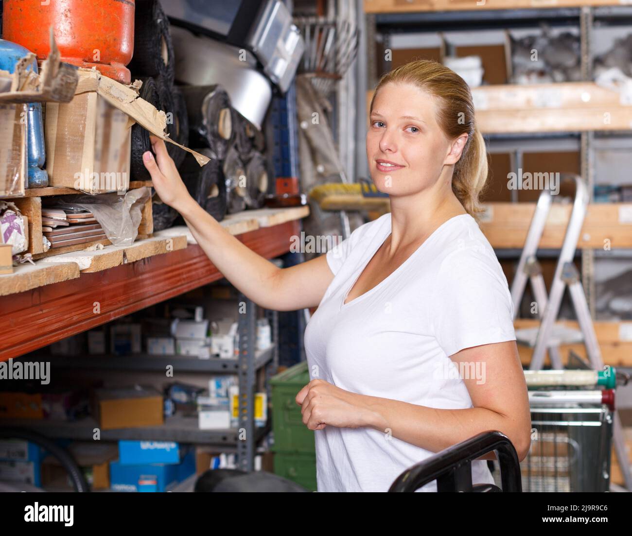 Positive young woman looking tools with note list in build store Stock ...