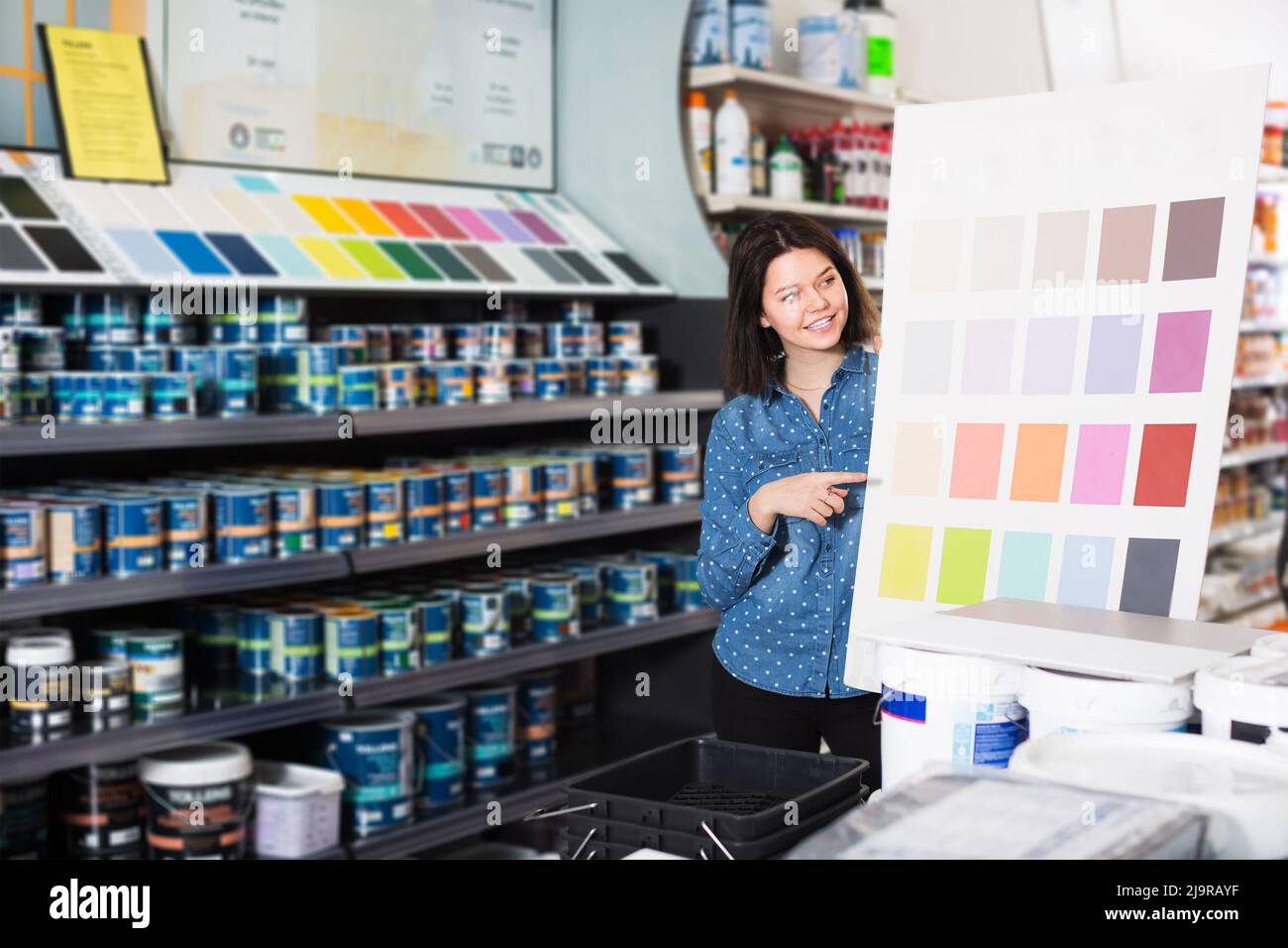 young female customer examining color scheme variants in paint store ...