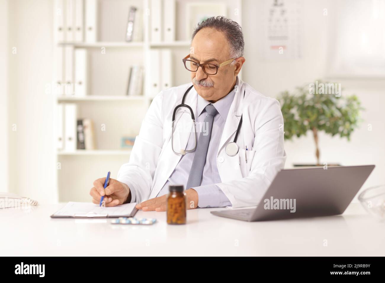 Mature doctor sitting in an office in front of a laptop computer and ...