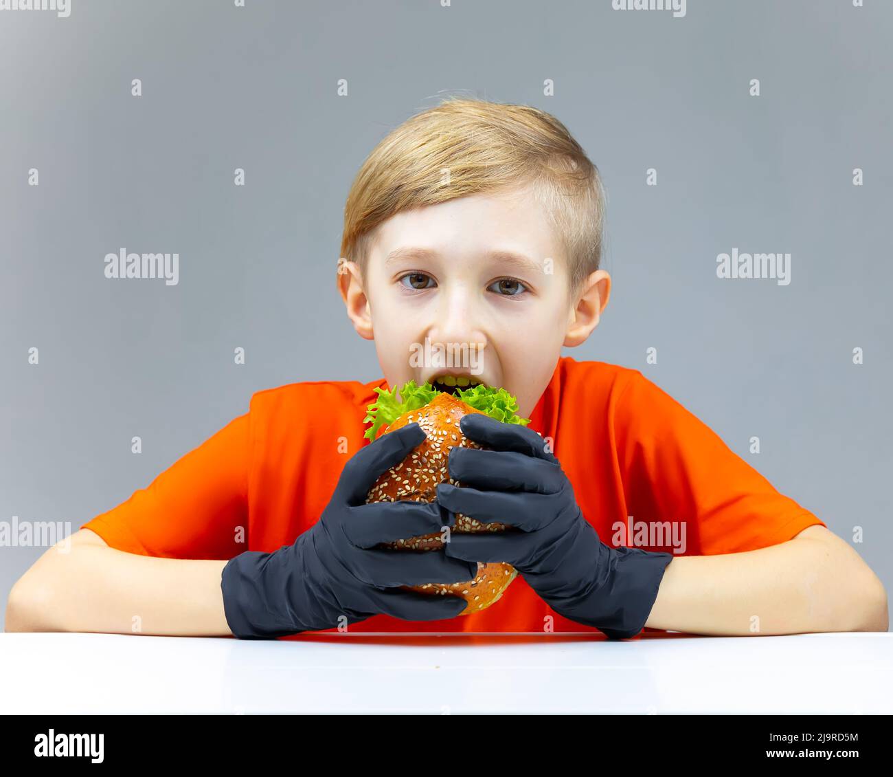a boy sitting at a table holds a juicy fried burger in front of him ...