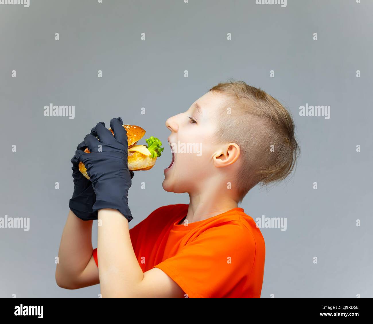 a boy standing sideways holding a huge burger in front of him. He ...