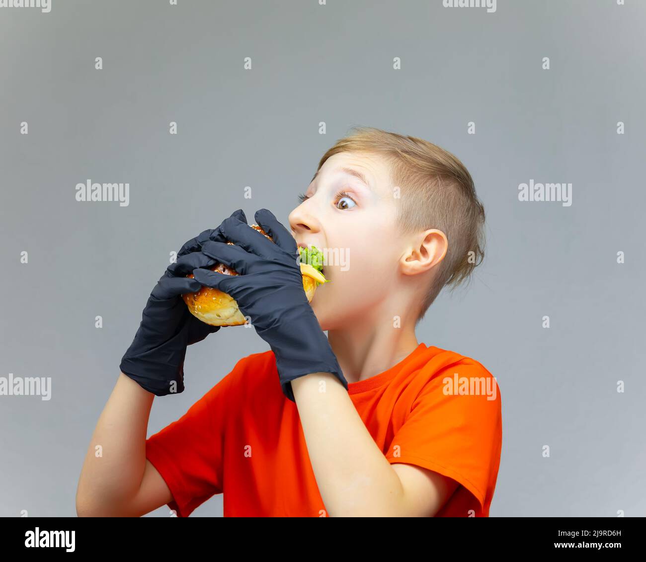 the boy bulged his eyes and bites a huge juicy burger with a salad ...