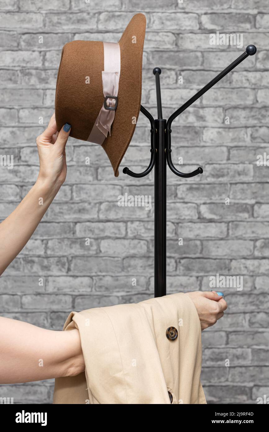 woman taking off hat from hanger holding raincoat in other hand. High ...