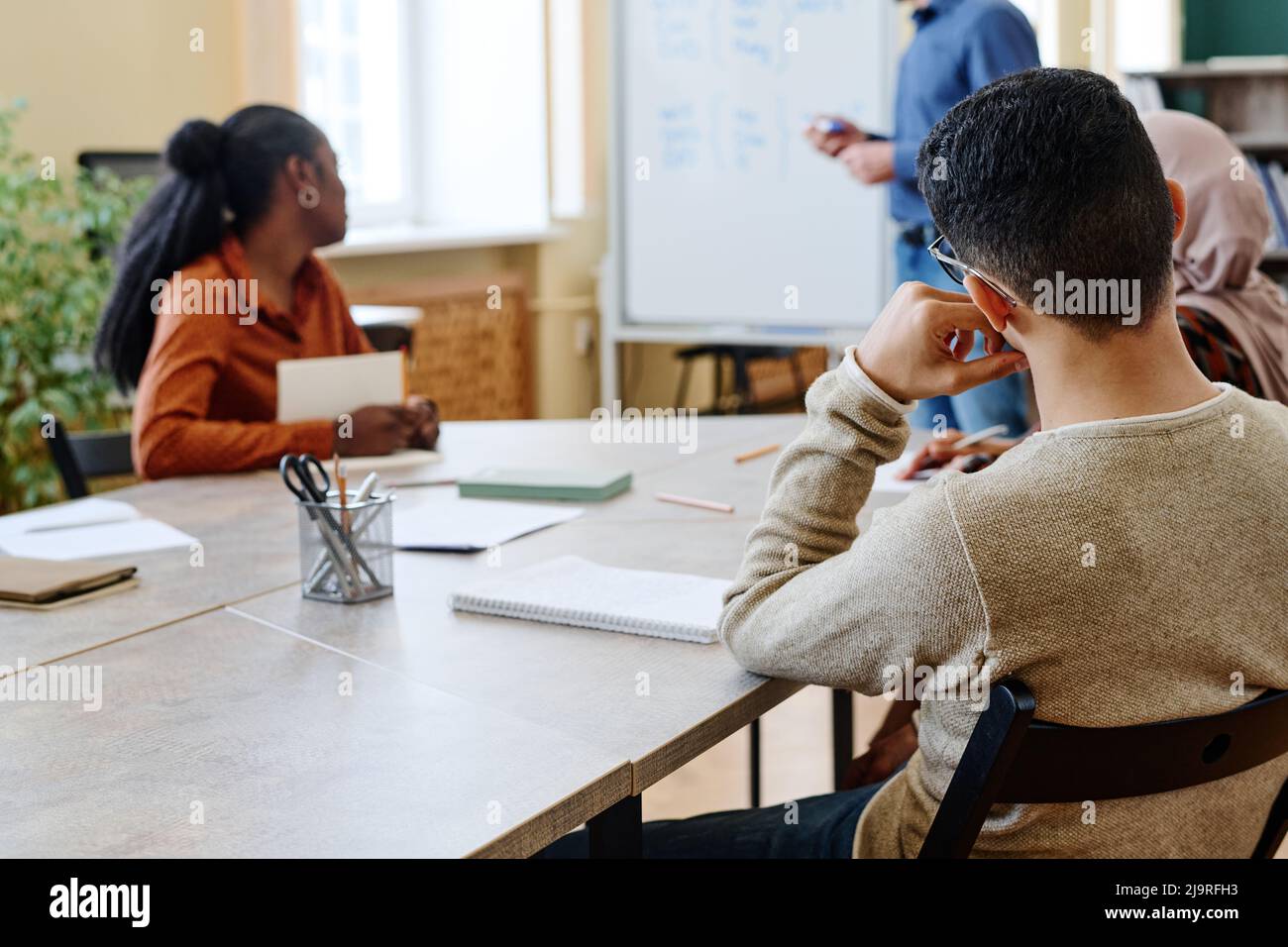 Unrecognizable multi-ethnic man and women sitting at table listening to ...