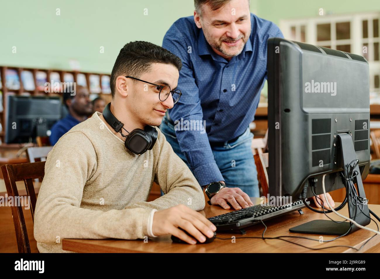 Cheerful mature teacher watching task his student finishing doing using ...