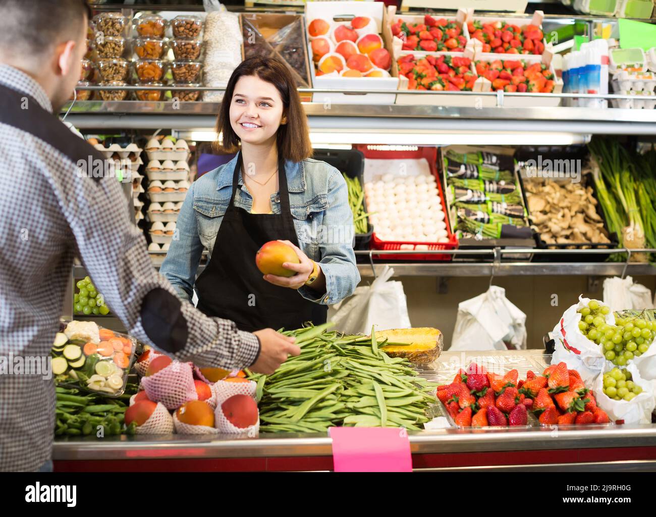 Female shopping assistant helping customer to buy fruit and vegetables ...