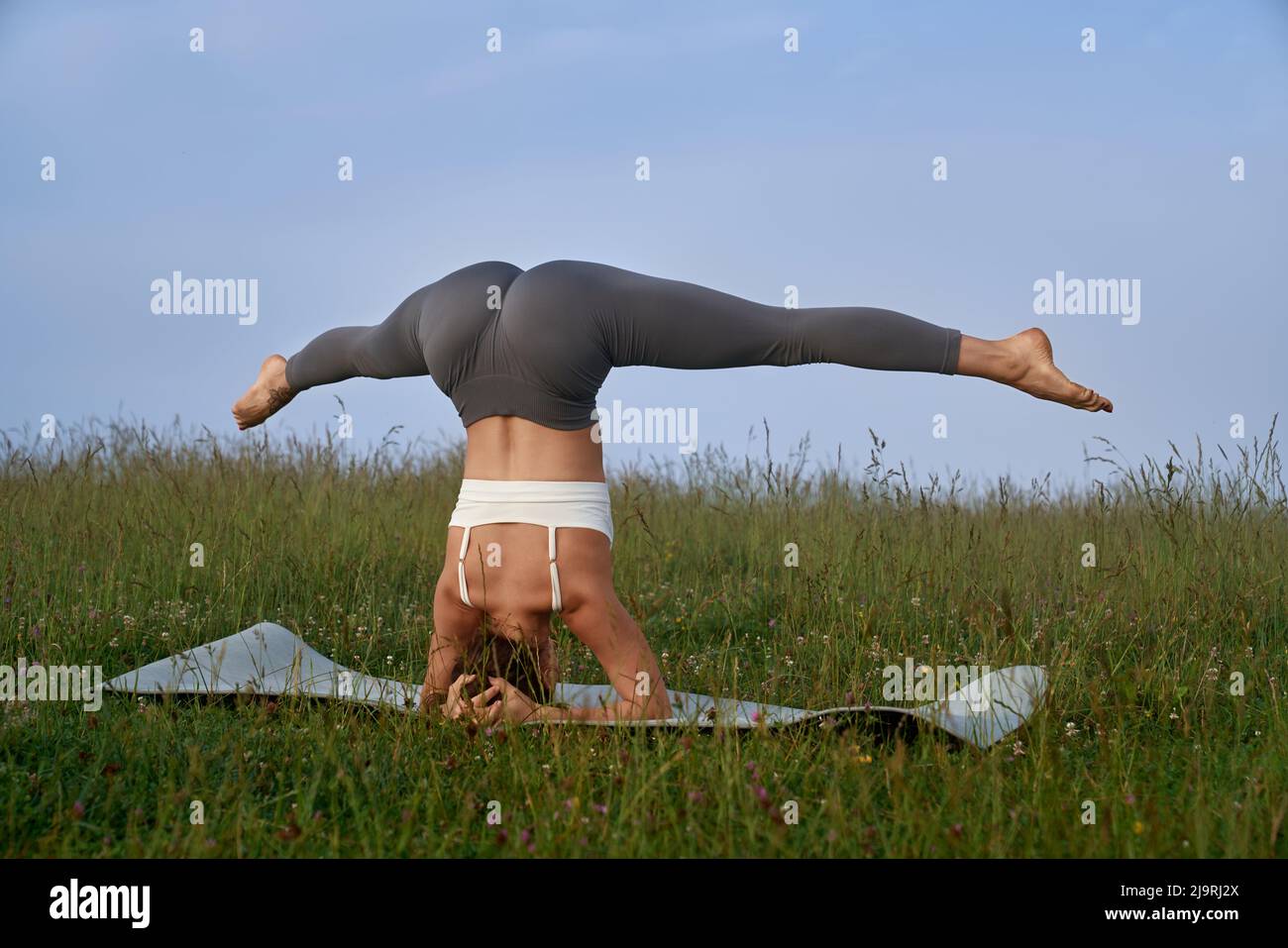 Back view of athletic strong woman standing on head on yoga mat among ...