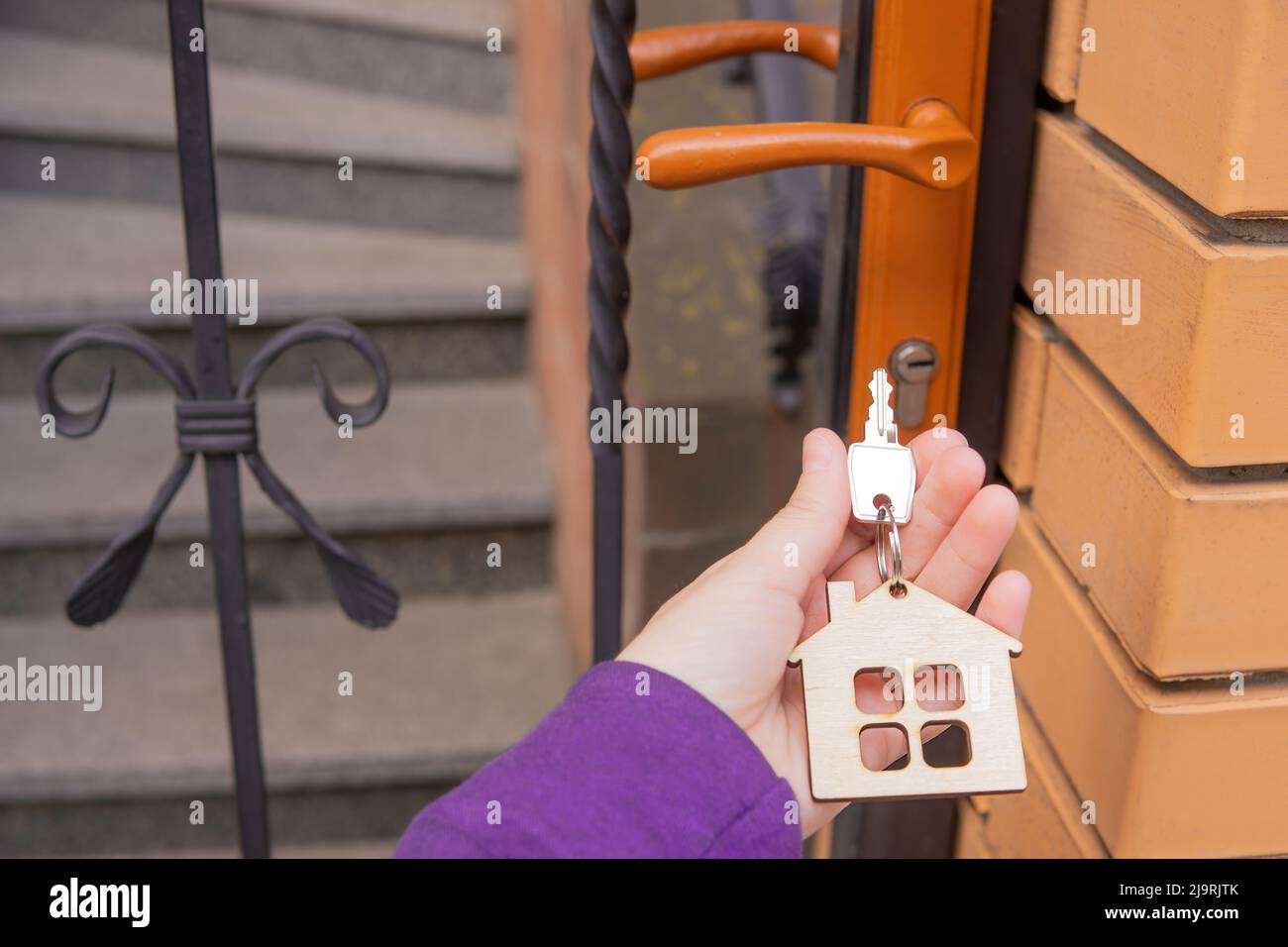 Female using a key with a house shaped keychain to open the house front ...