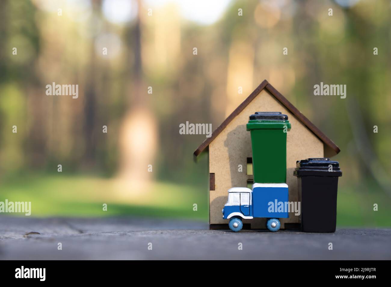 Toy garbage truck and garbage cans standing close to a miniature house ...
