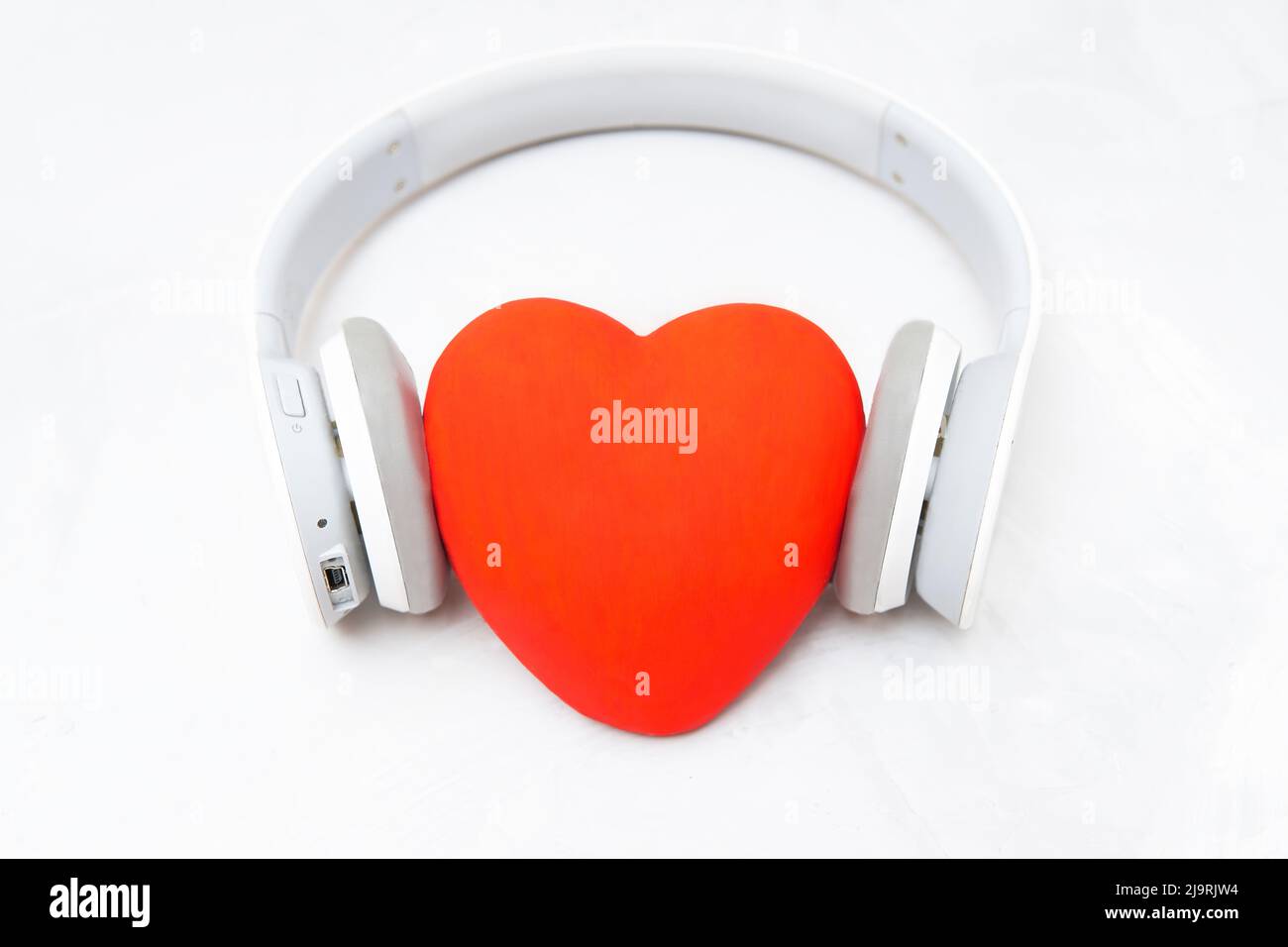 Wireless headphones put over a large red heart on a neutral background ...