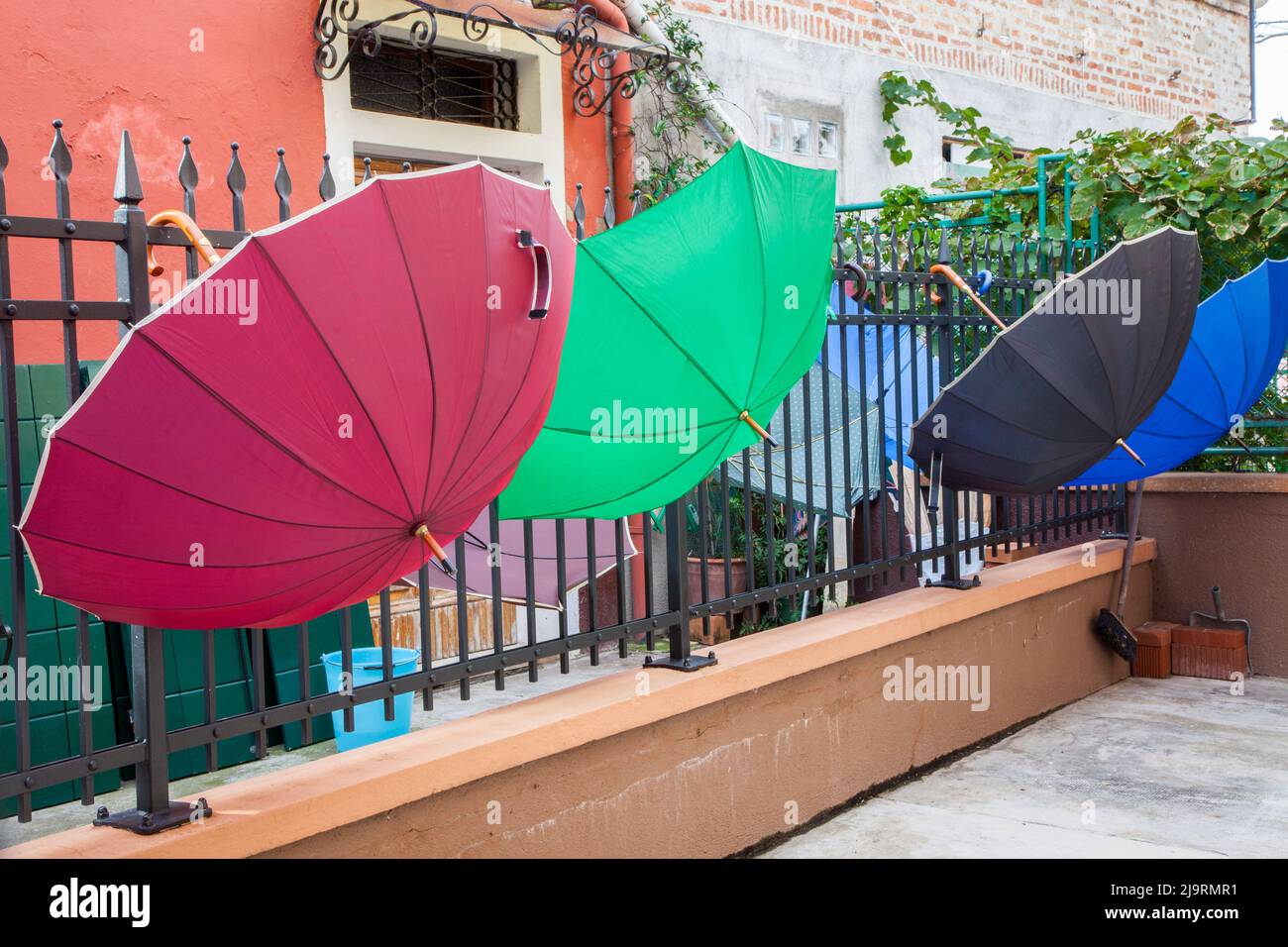 Italy, Venice, Burano Island. Colorful umbrellas hanging on a railing ...