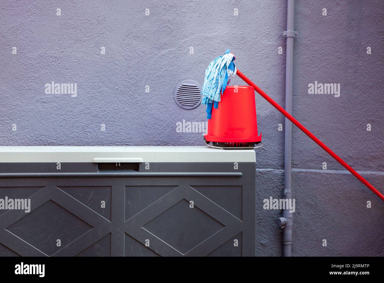 Italy, Venice, Burano Island. Red mop and bucket against a purple wall ...