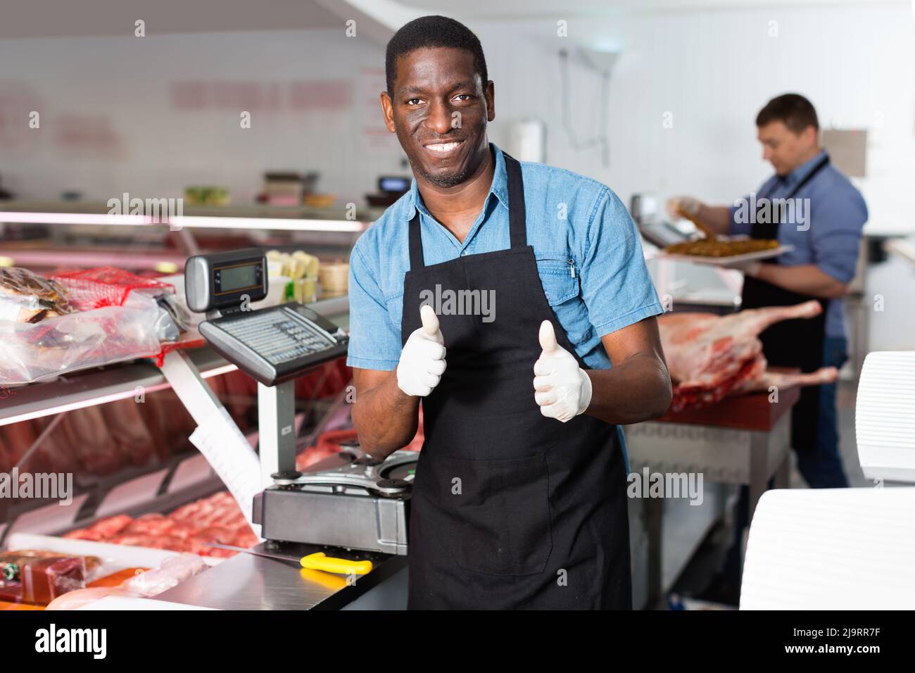 Happy African American seller of butcher store standing behind counter ...
