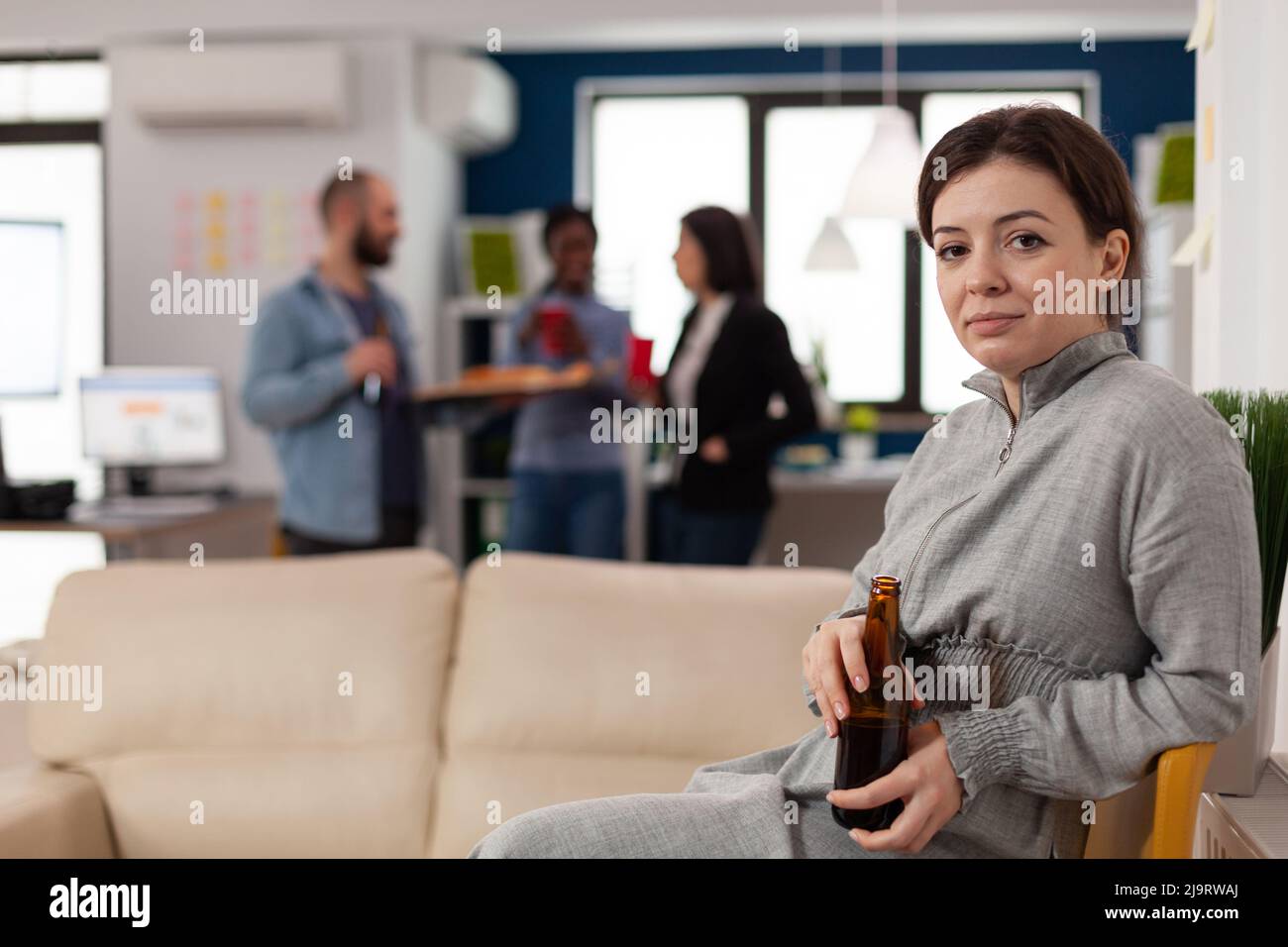 Portrait of young woman holding beer bottle after hours in office ...