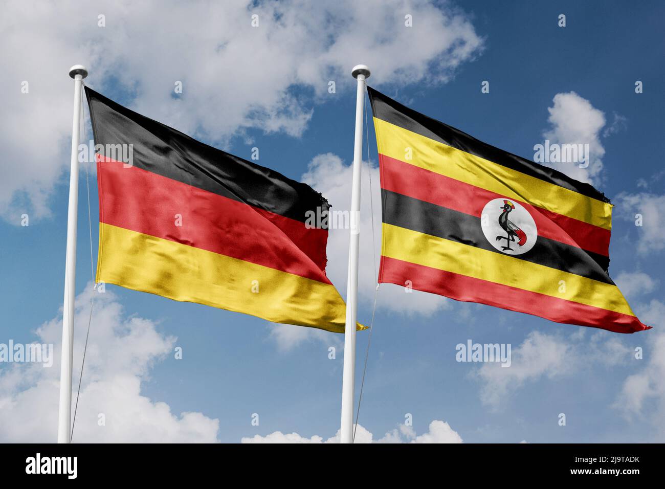 Germany and Uganda two flags on flagpoles and blue cloudy sky ...