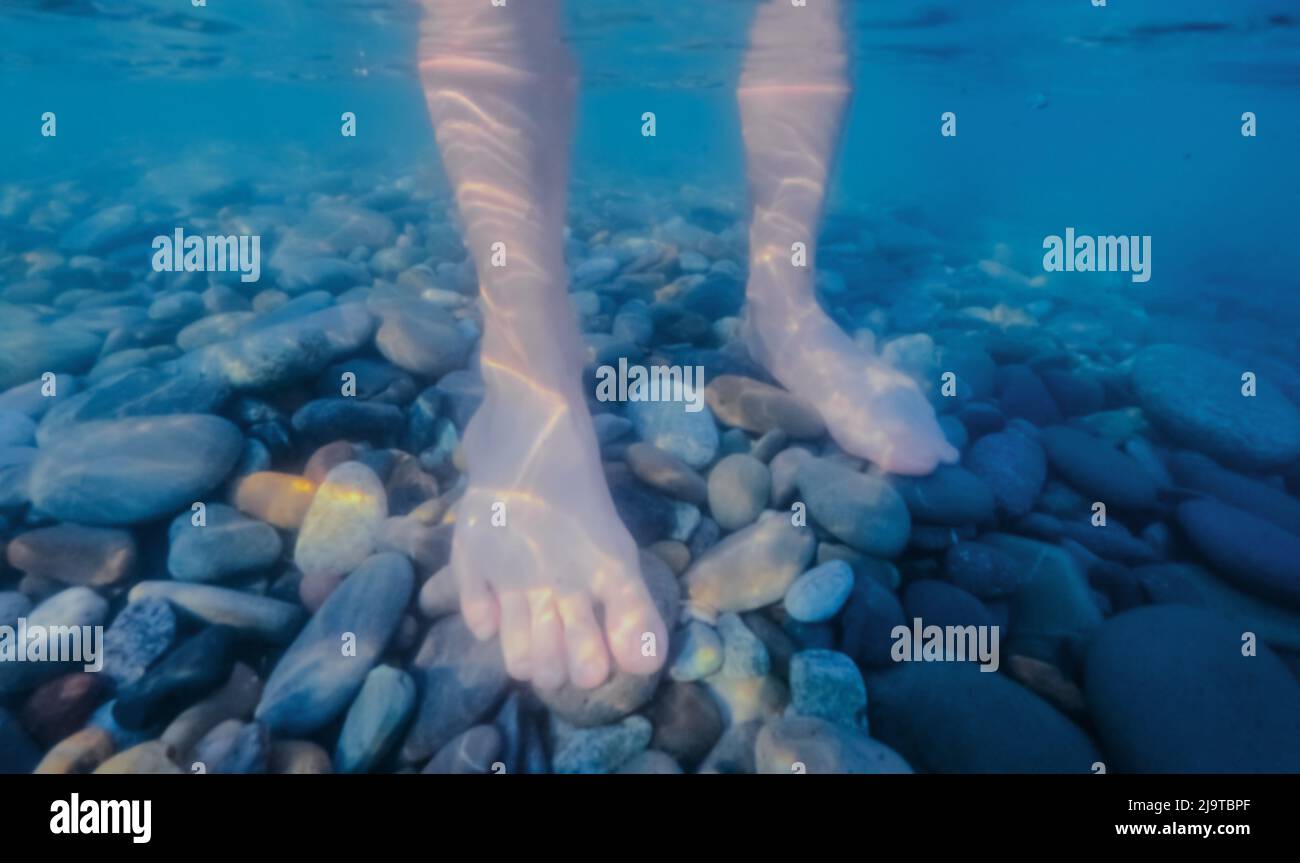 Women's feet standing on a pebbly bottom in sea water. Underwater photo ...