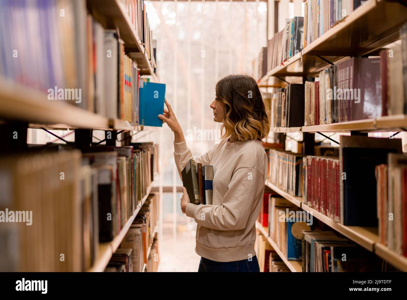Beautiful girl taking a book while standing in a library Stock Photo ...