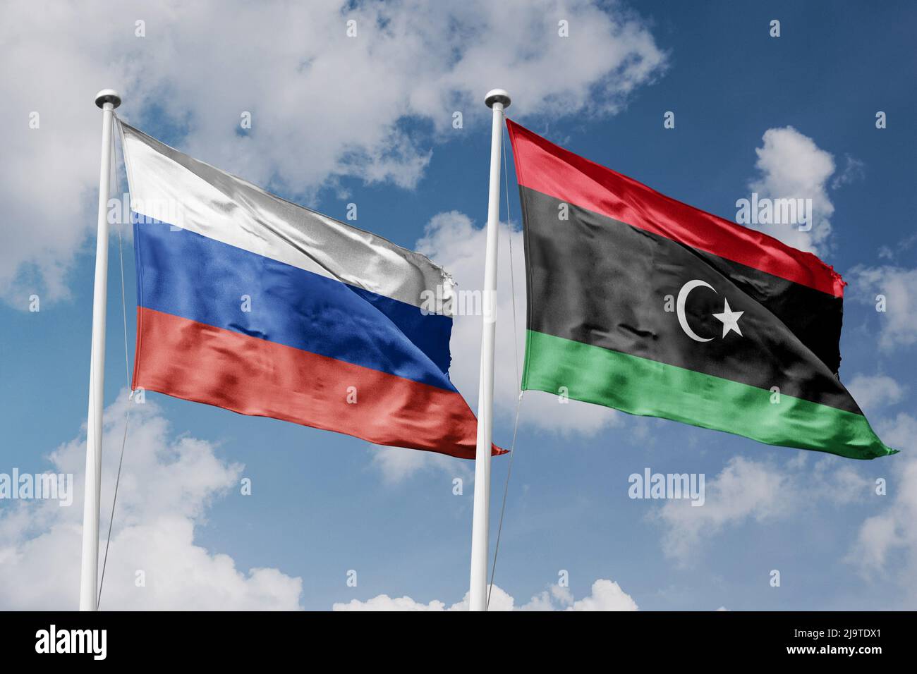 Russia and Libya two flags on flagpoles and blue cloudy sky background ...