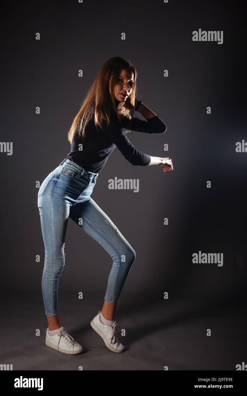 Side full-body portrait of a young female model in black top and jeans ...