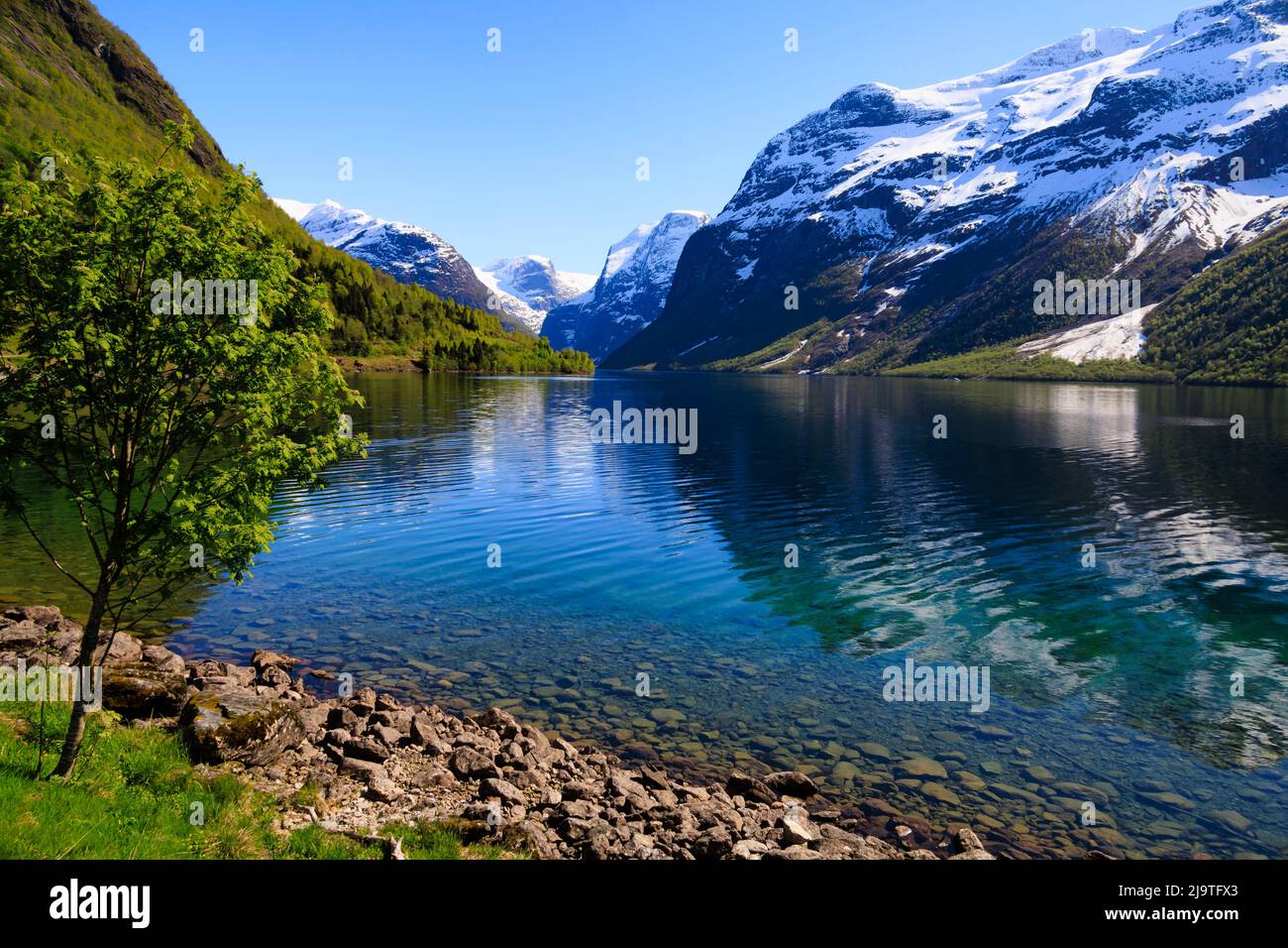 Crystal Clear, blue water in Lake Lovatnet with snow capped mountains ...