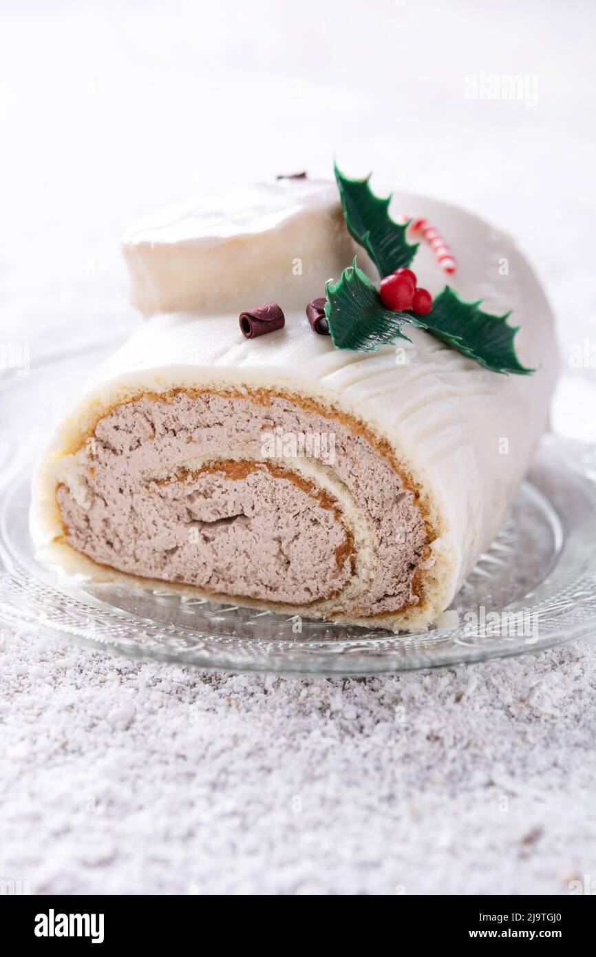 White chocolate yule log cake with ornament on wooden table and snow ...