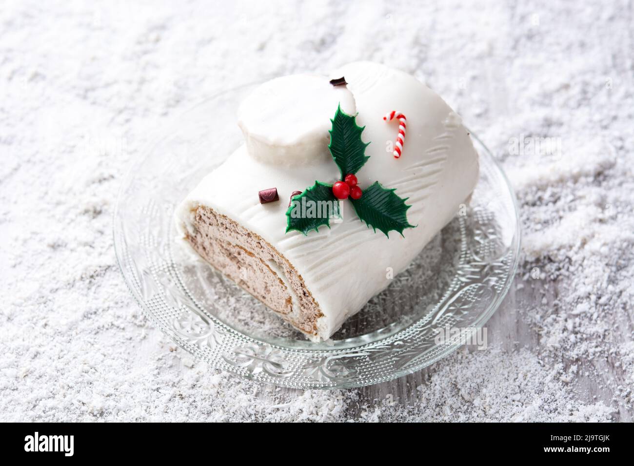 White chocolate yule log cake with ornament on wooden table and snow ...