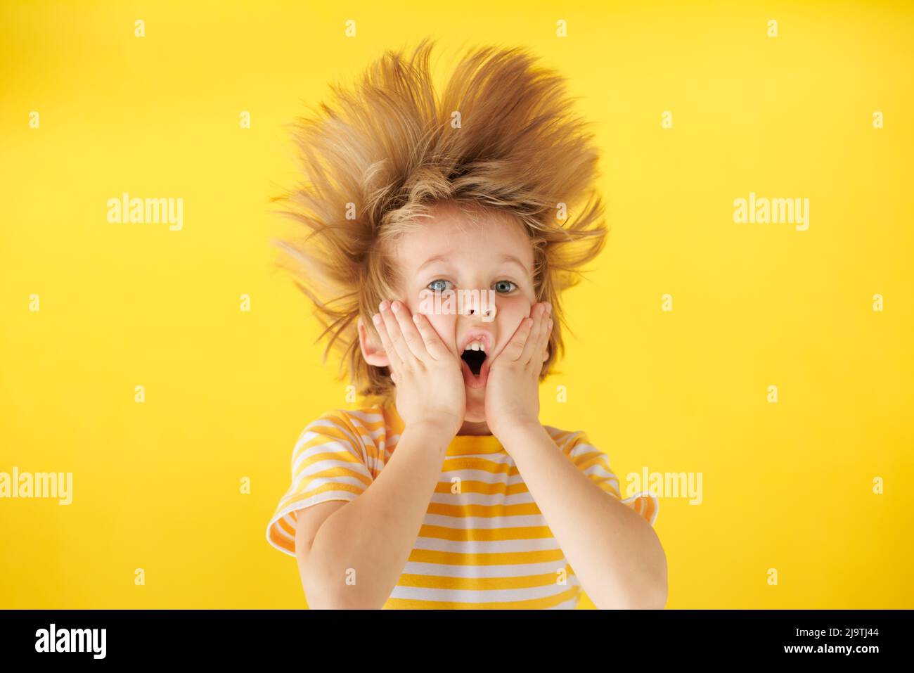 Surprised child holding face. Shocked kid against yellow background ...