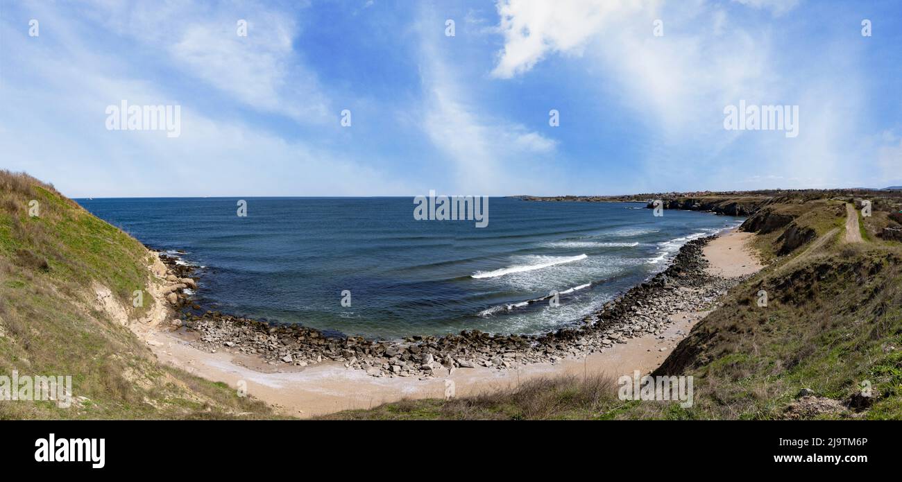Panorama of a wild stone and sandy beach with dark wet sea sand and ...