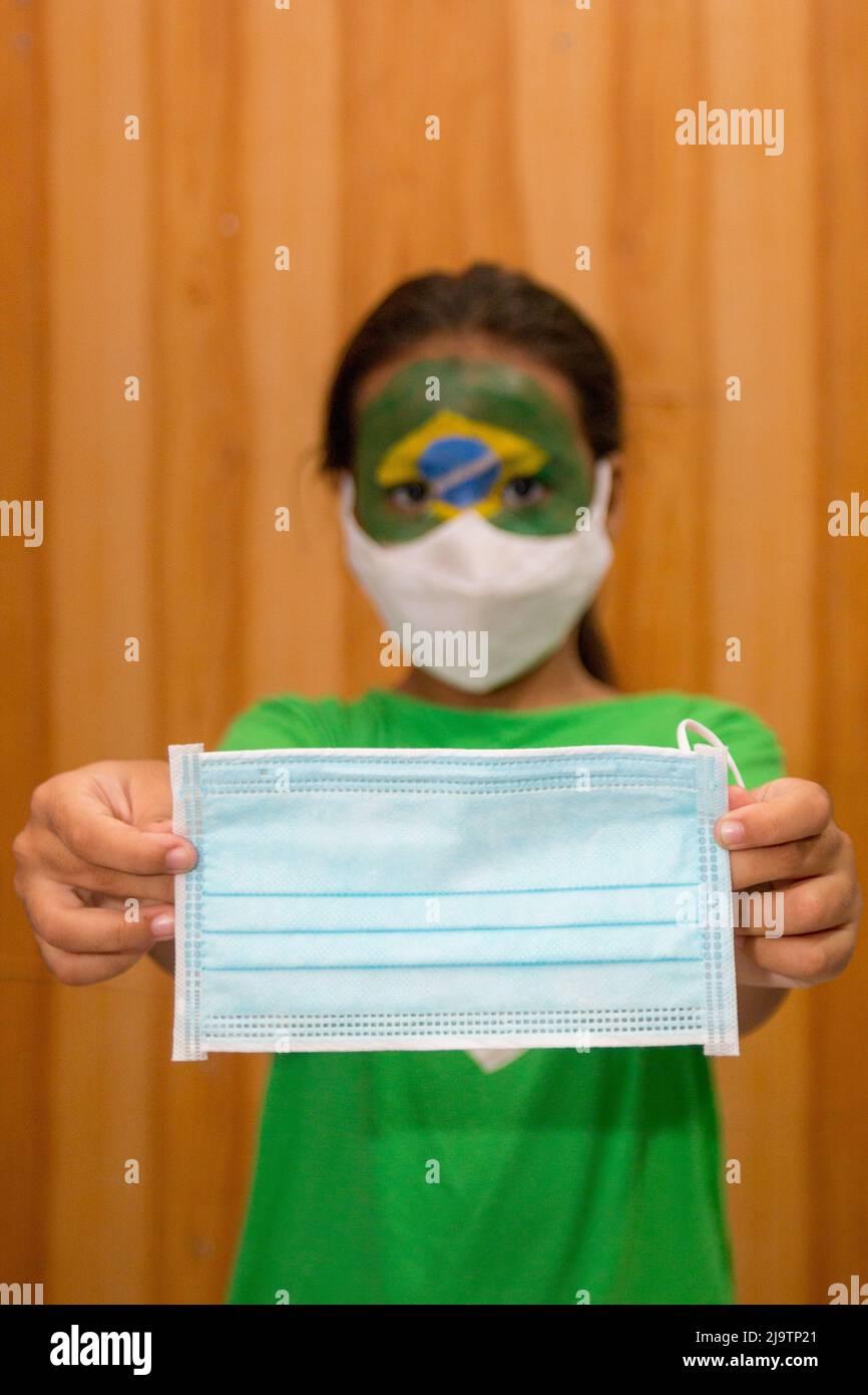 child with mask with face painted with the flag of brazil, holding a ...