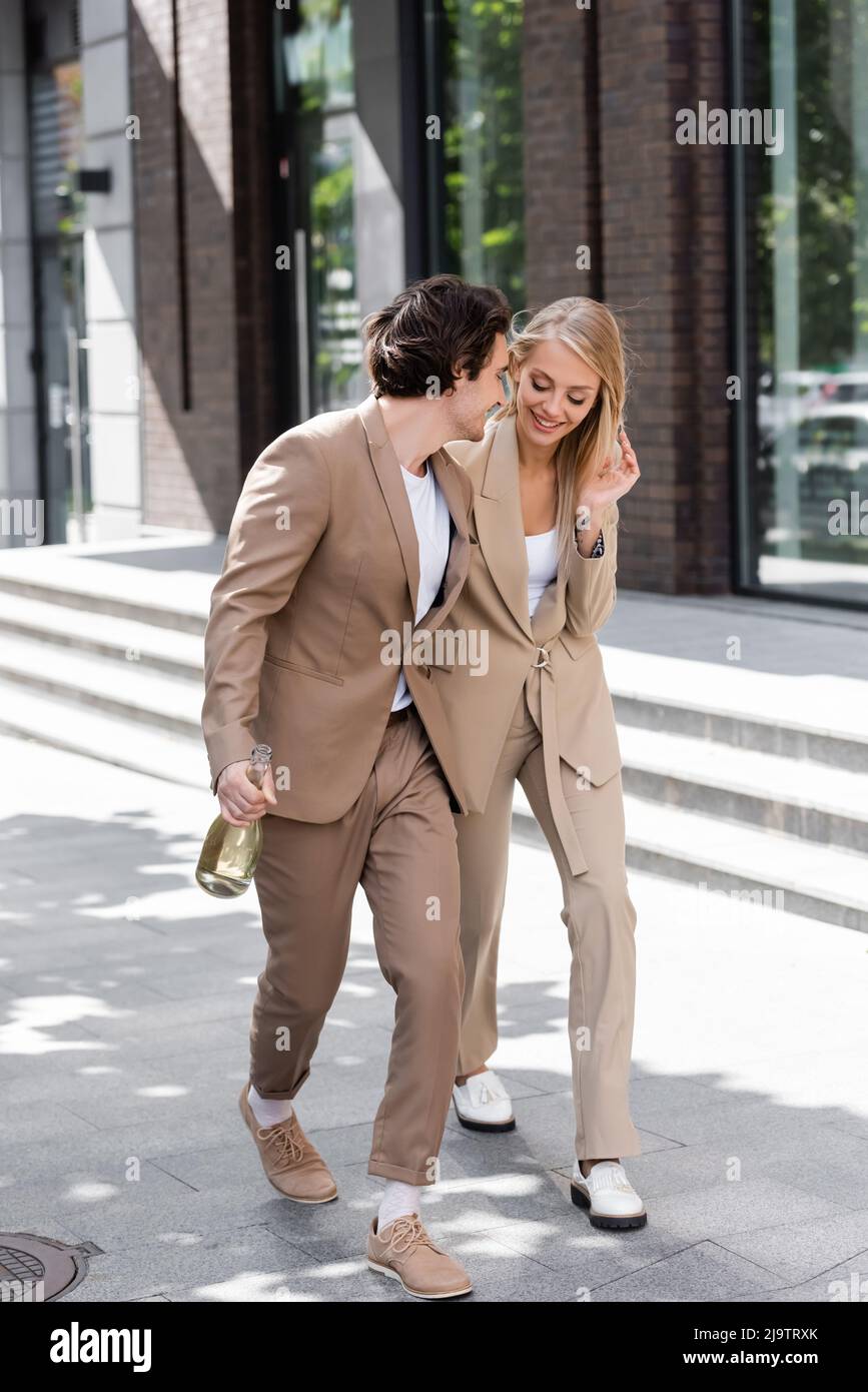 full length of young man with champagne bottle walking near blonde ...