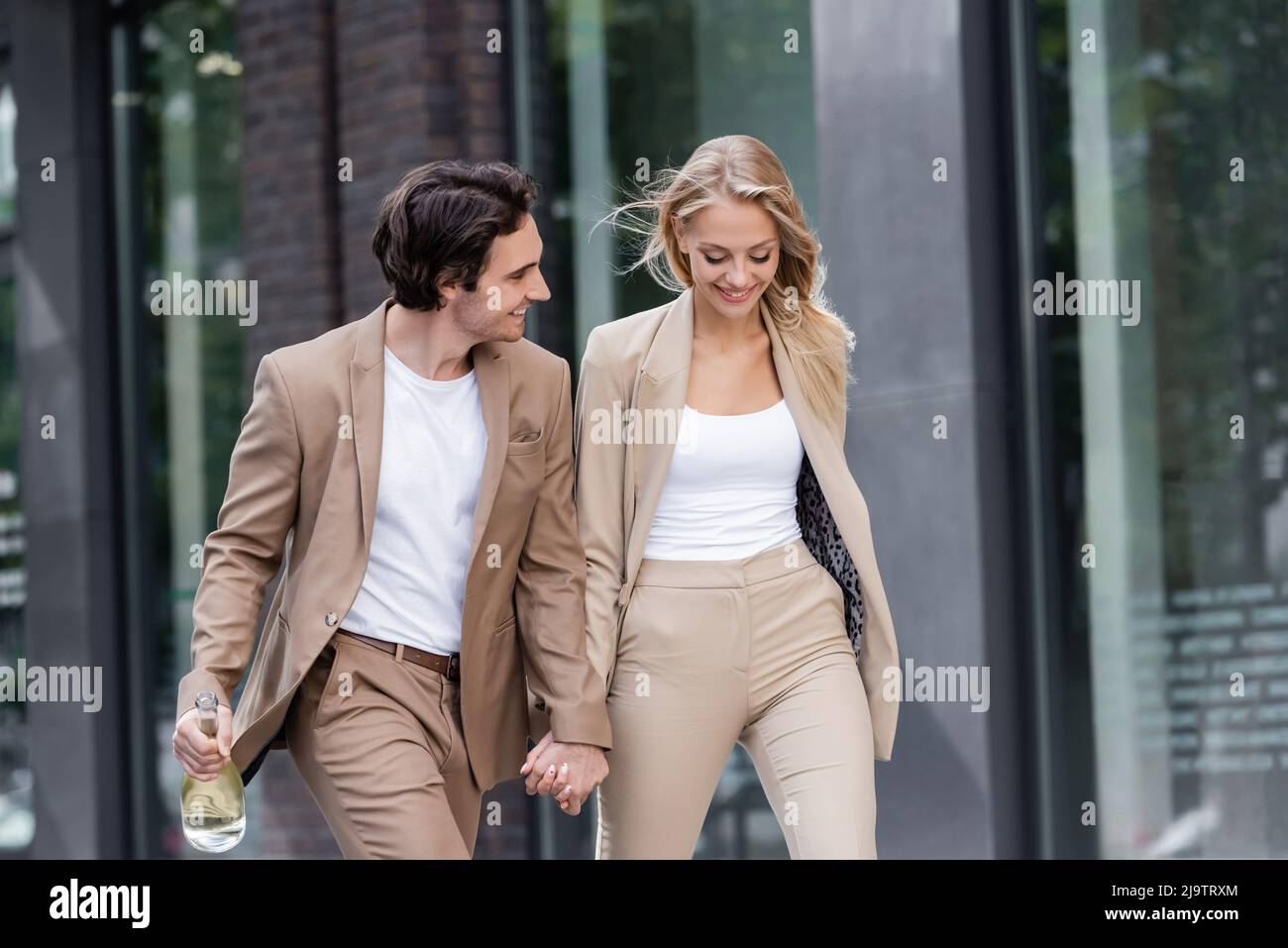 young man with champagne bottle holding hands with happy blonde woman ...
