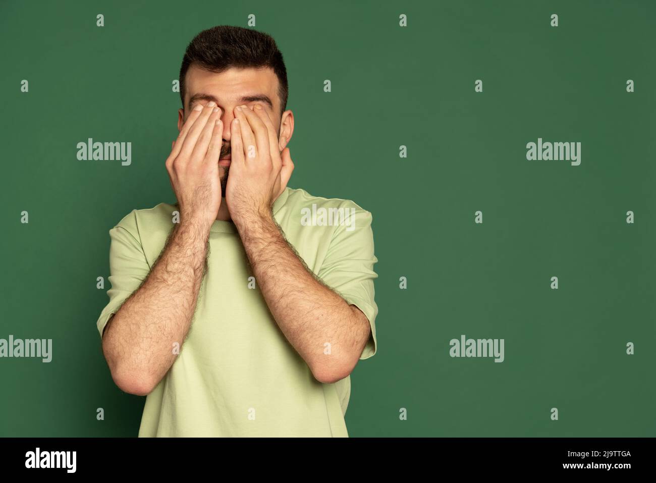 Portrait of young man closing eyes with hands, feeling sleepy and tired ...