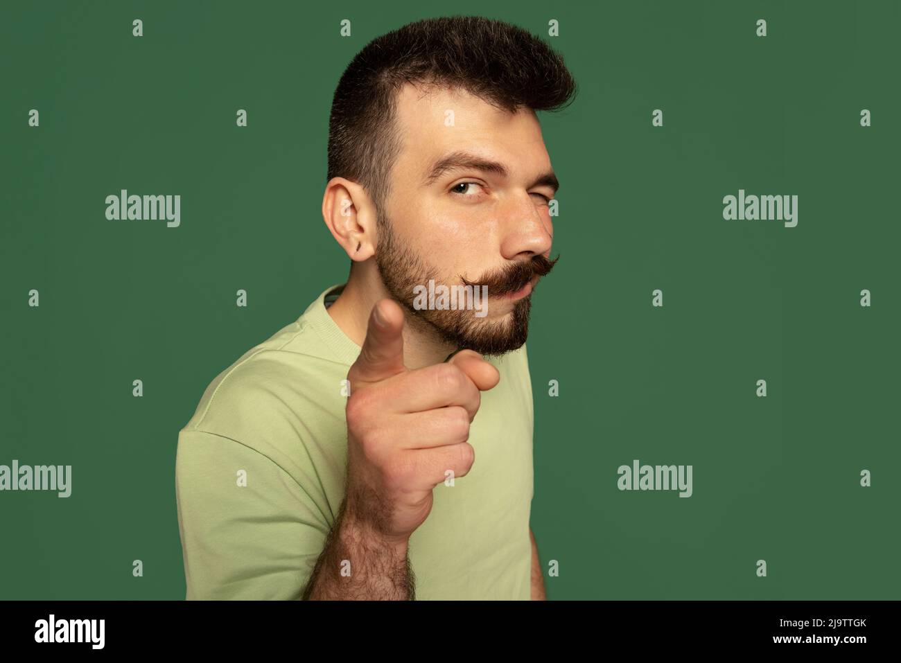 Portrait of young stylish man with moustache looking and pointing at ...