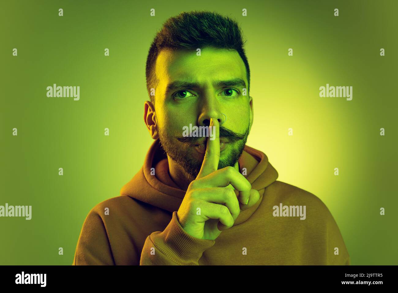Portrait of young man putting finger to lips, posing isolated over ...