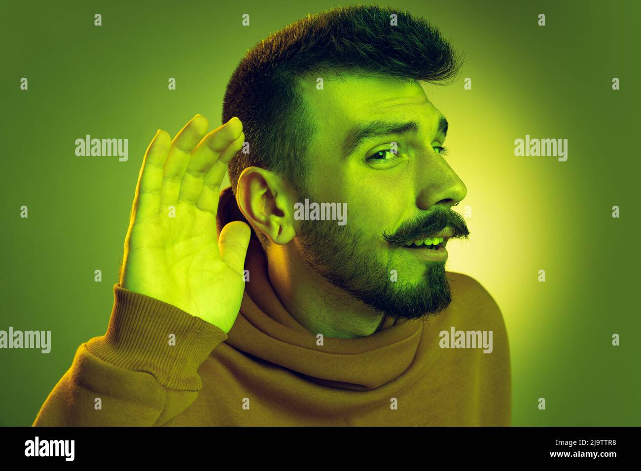 Portrait of young man with hand to ear posing isolated over green ...