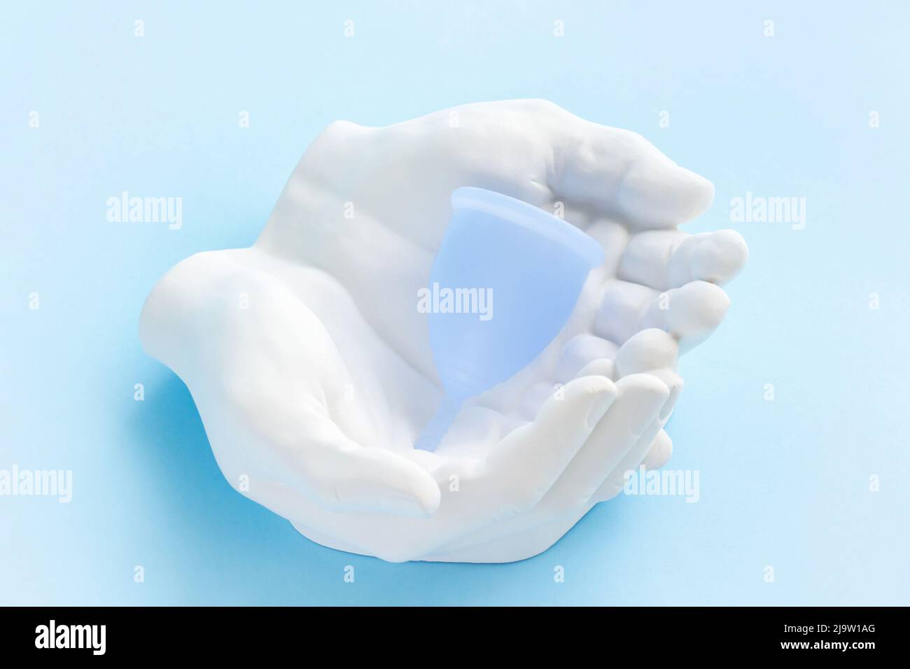 Blue menstrual cup in decorative plaster hands on blue background ...
