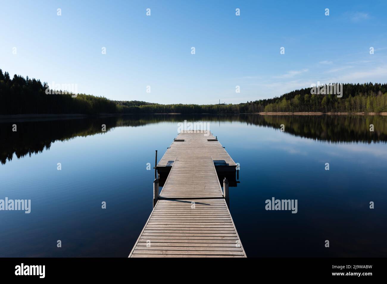 Wooden pier on a calm Lake with reflection in water on a sunny day in ...