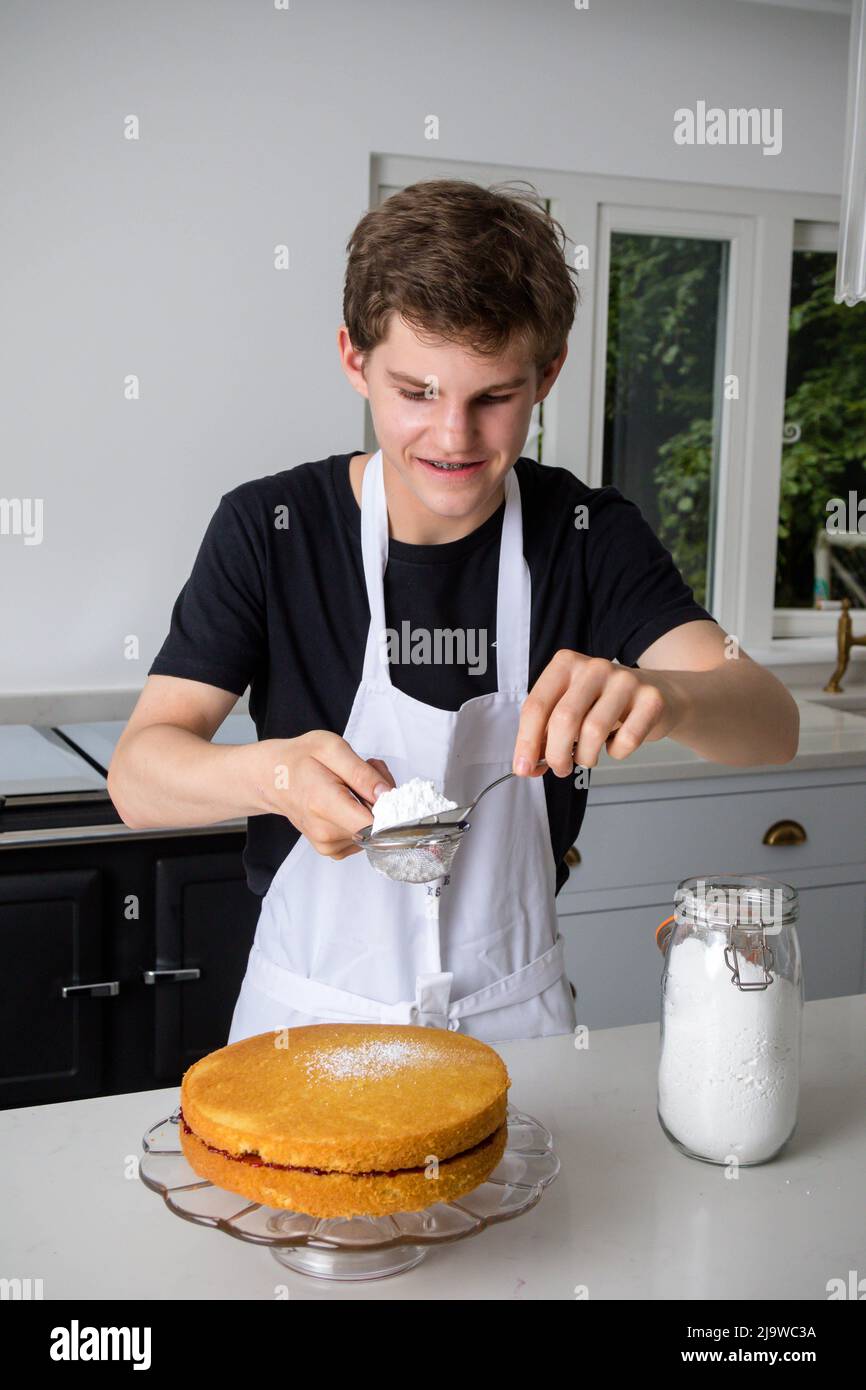A teenage boy in a domestic kitchen putting icing sugar on a cake Stock ...
