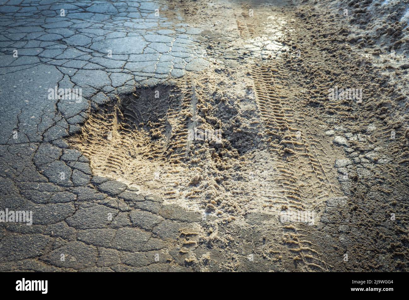 Large pit on the old country road in winter close-up. Mud and snow ...