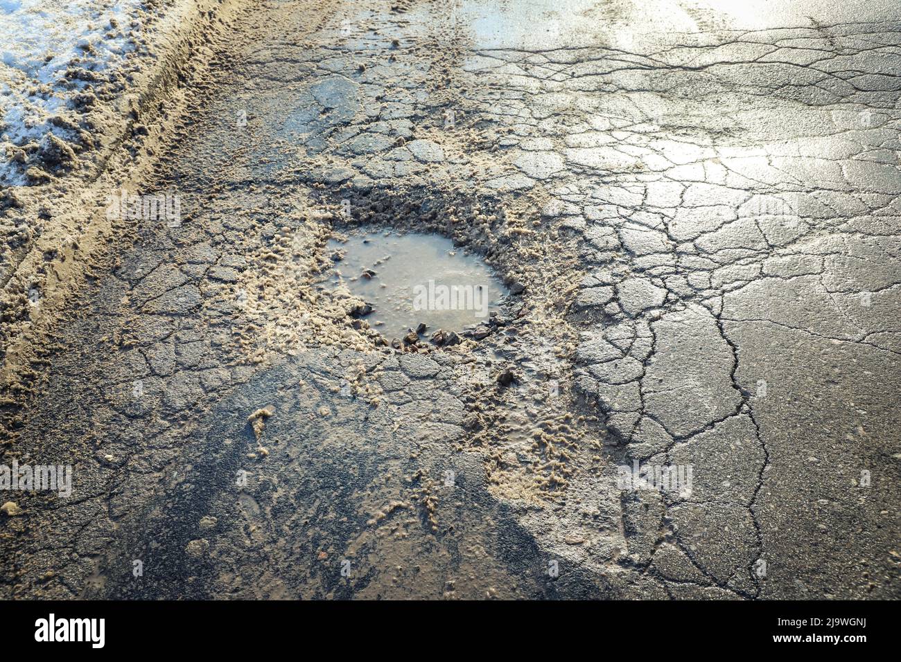 Large pit on the old country road in winter close-up. Mud and snow ...