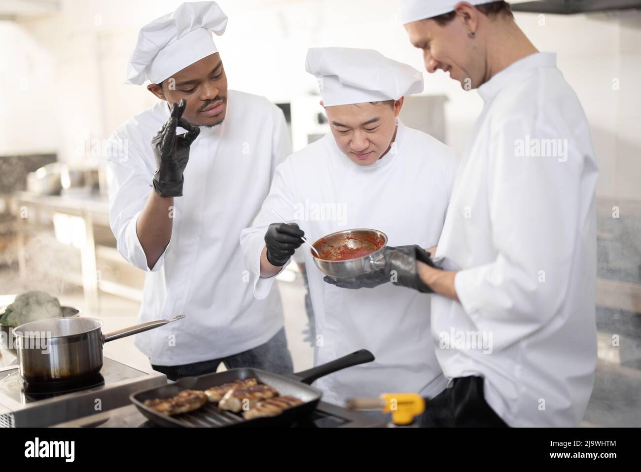 Three chef cooks with different ethnicities tasting sauce with a spoon ...