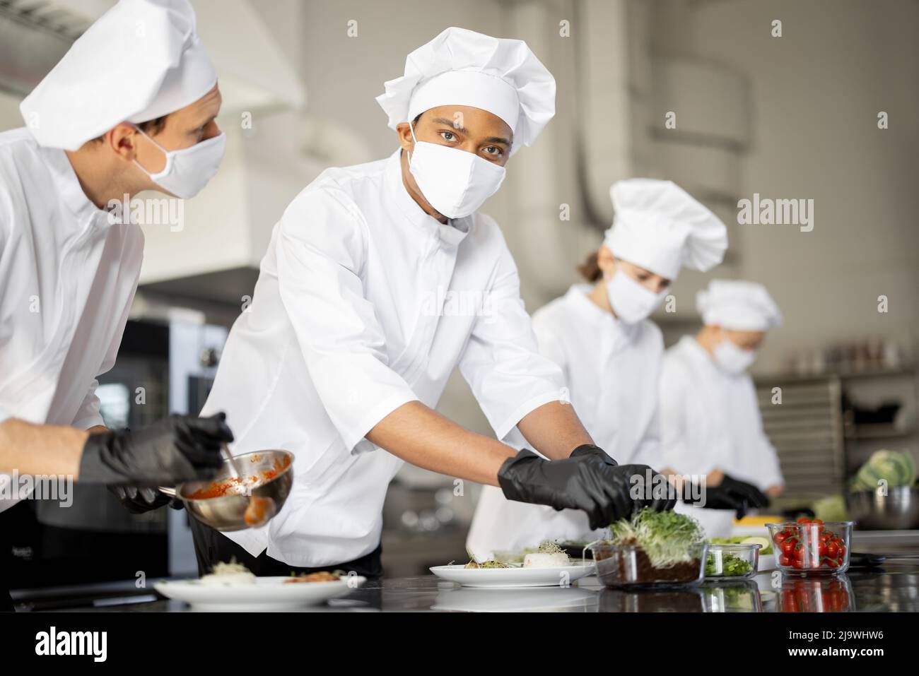 Multiracial group of cooks finishing main courses while working ...