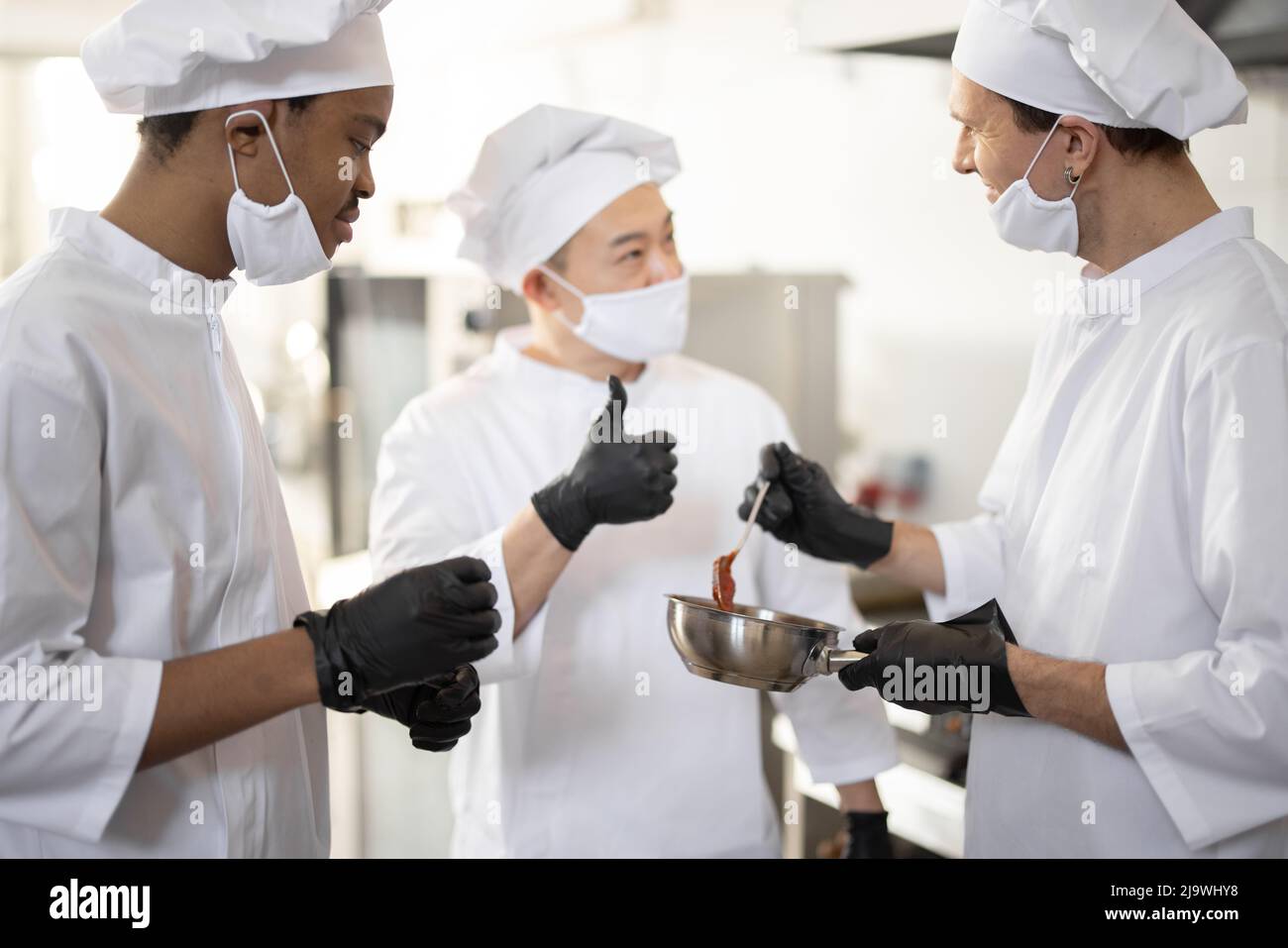 Three chef cooks with different ethnicities tasting sauce with a spoon ...