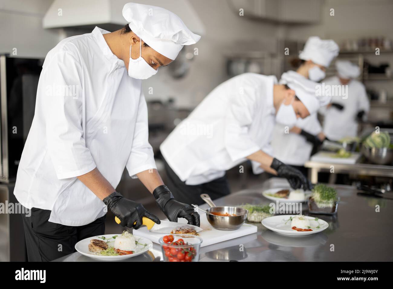 Multiracial group of cooks finishing main courses while working ...