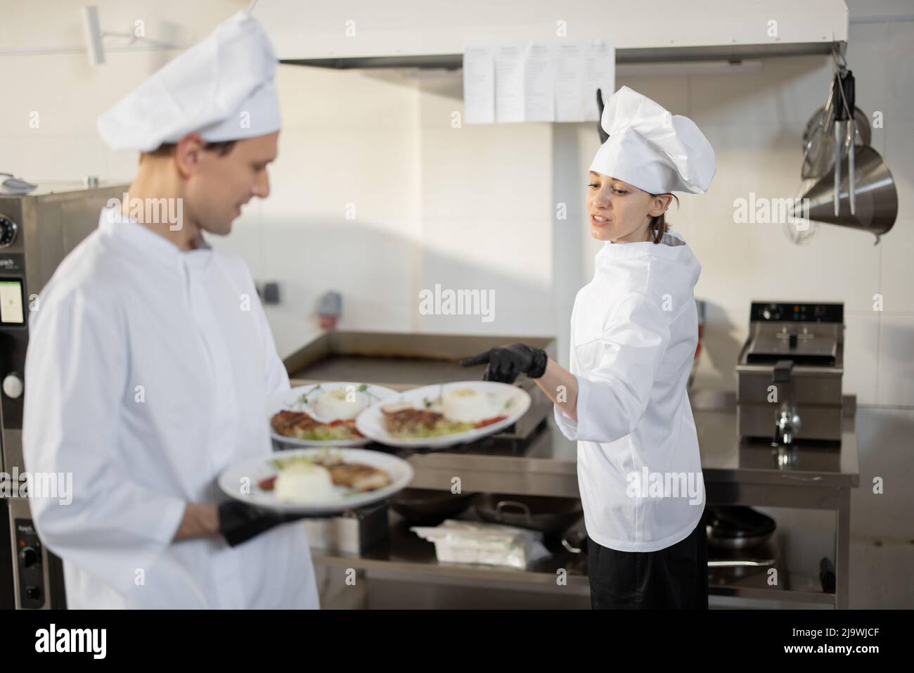 Chef standing with ready meals, talking with female cook in the kitchen ...